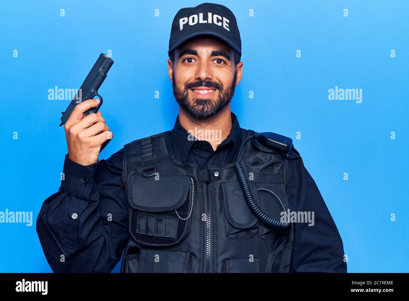 Young hispanic man wearing police uniform holding gun looking positive ...