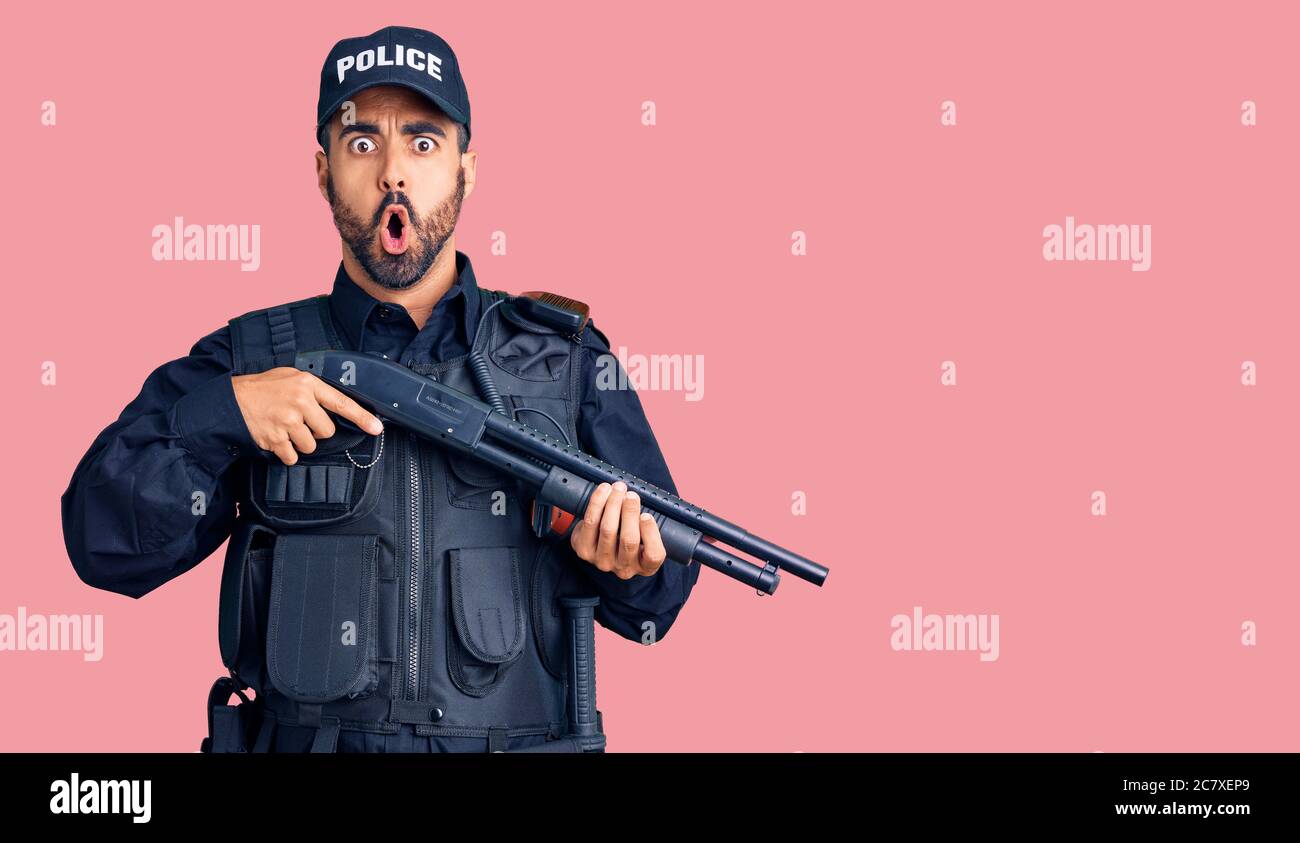 Young hispanic man wearing police uniform holding shotgun scared and ...