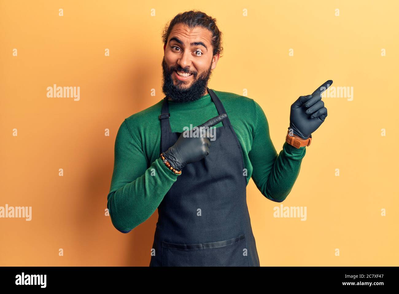 Young arab man wearing barber apron smiling and looking at the camera ...