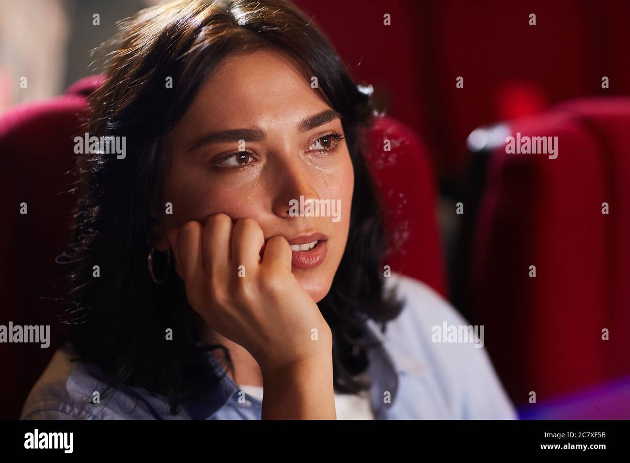 Head and shoulders portrait of young woman crying in cinema while ...