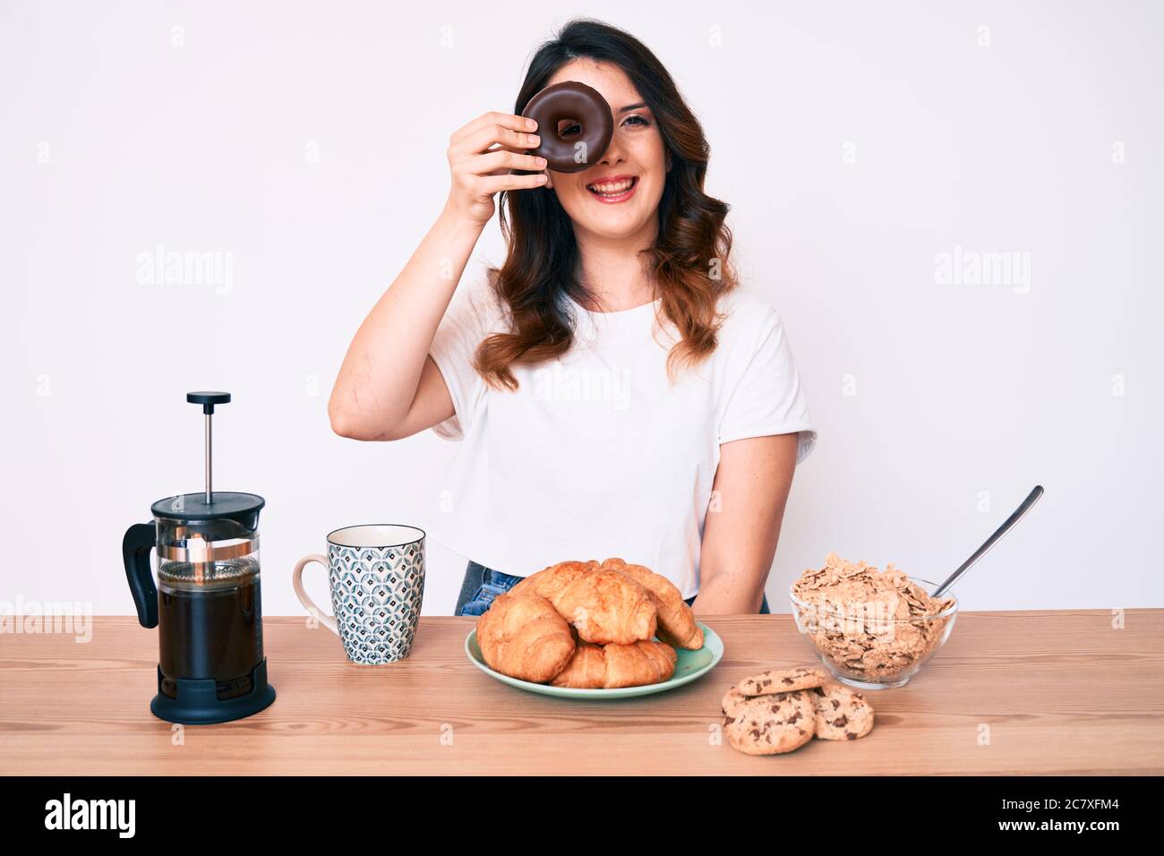 Young beautiful brunette woman eating breakfast holding cholate donut ...