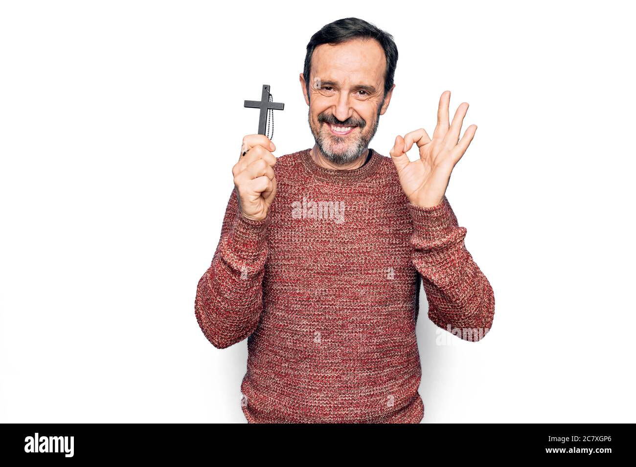 Middle age handsome catholic man praying holding christian cross over ...
