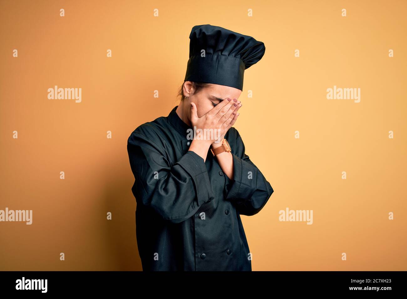 Young beautiful chef woman wearing cooker uniform and hat standing over ...