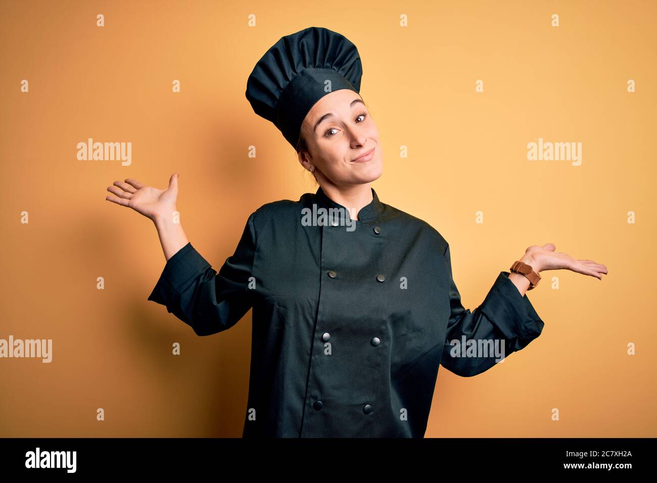 Young beautiful chef woman wearing cooker uniform and hat standing over ...