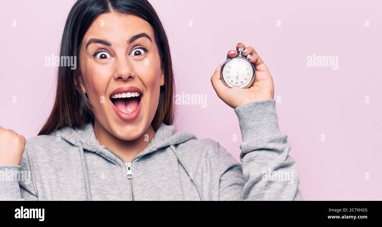 Young beautiful brunette sporty woman holding stopwatch over isolated ...