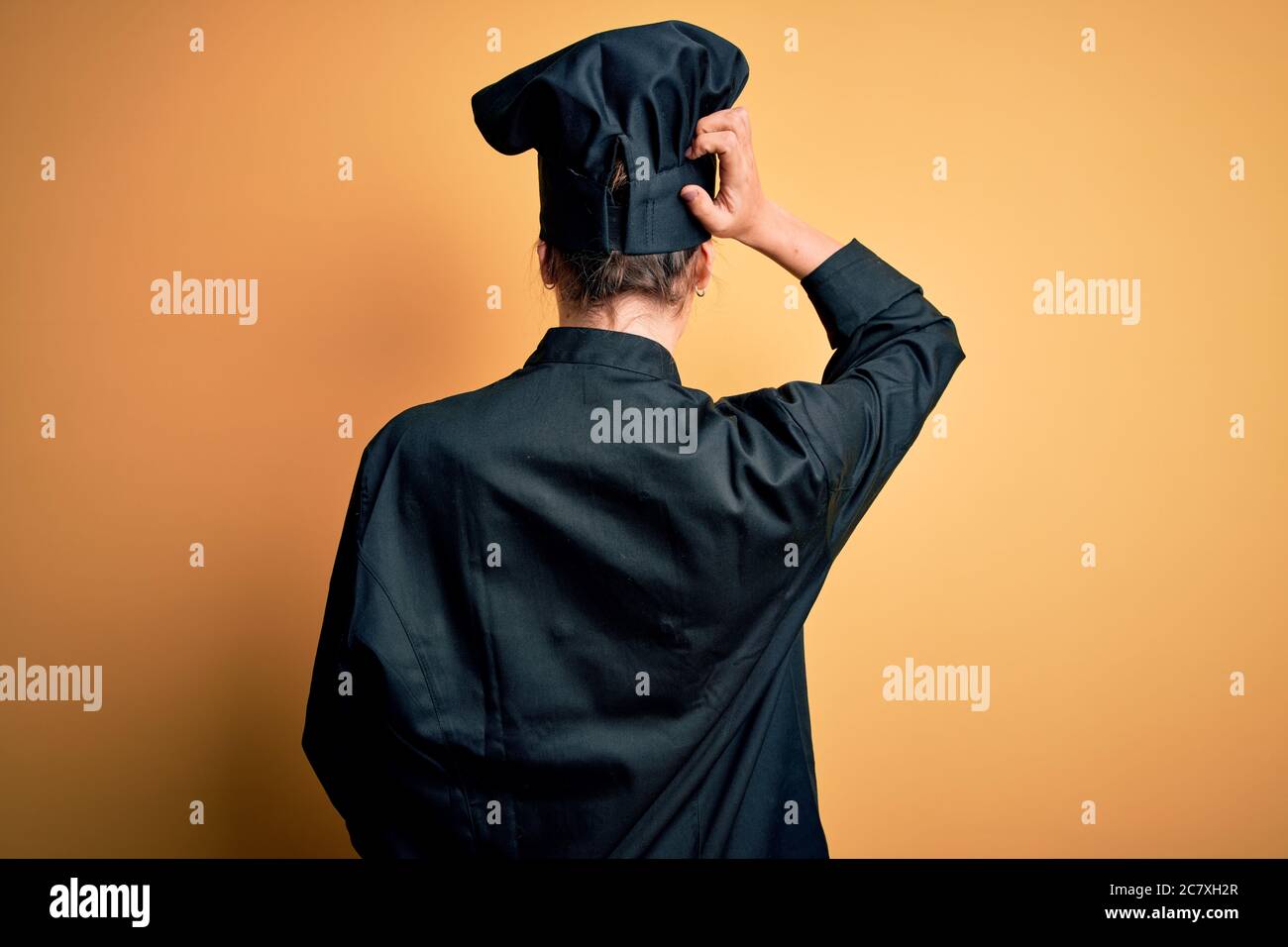 Young beautiful chef woman wearing cooker uniform and hat standing over ...