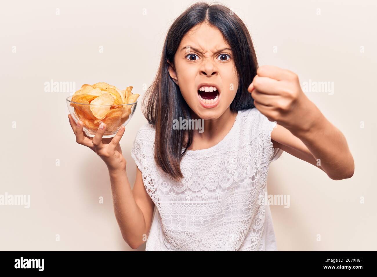 Beautiful child girl holding potato chip annoyed and frustrated ...