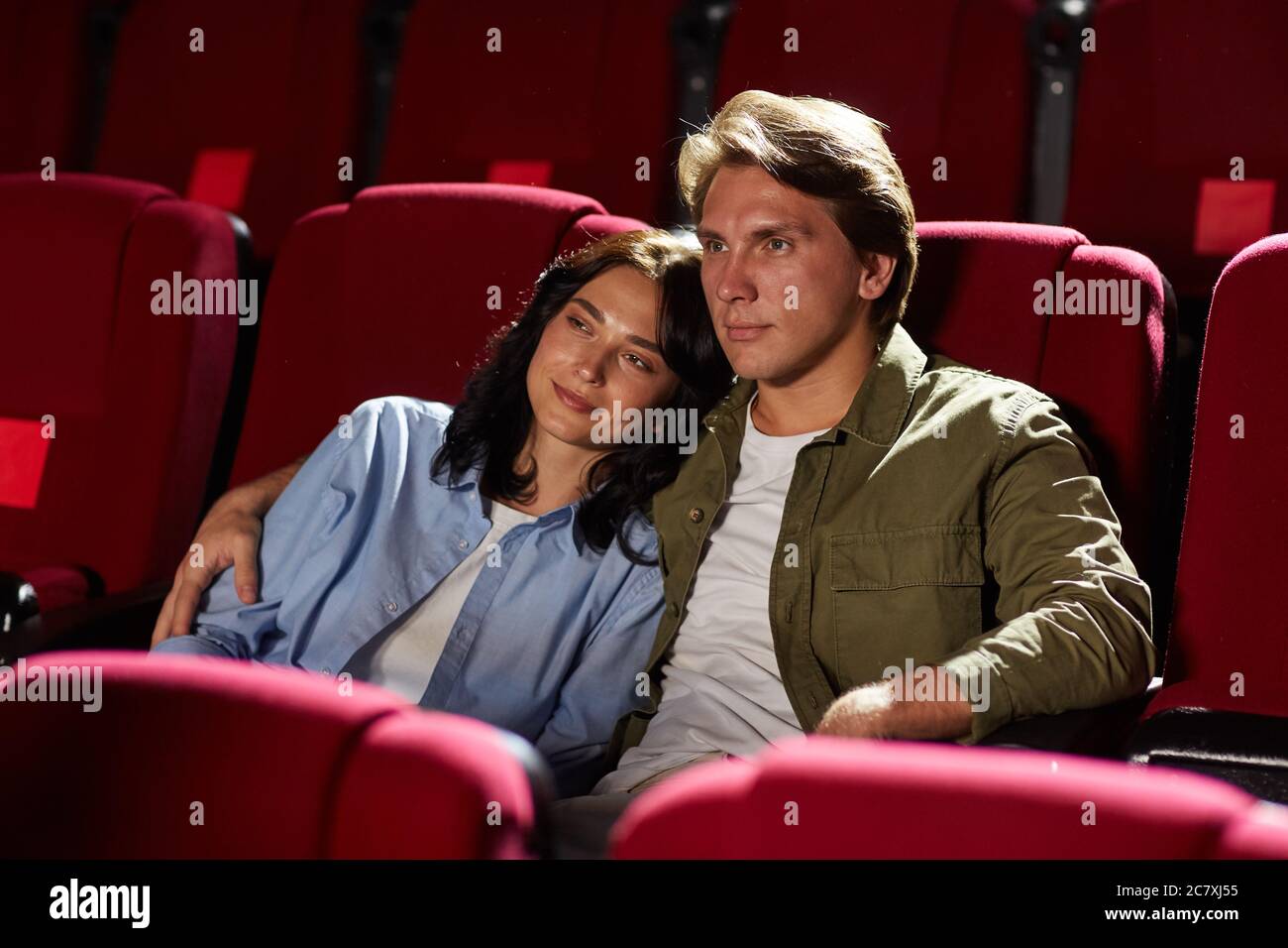 Portrait of young loving couple in cinema watching movie while enjoying ...