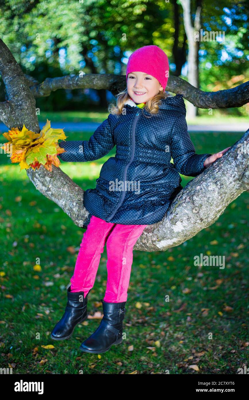 cute happy little girl sitting on tree branch in autumn park Stock ...