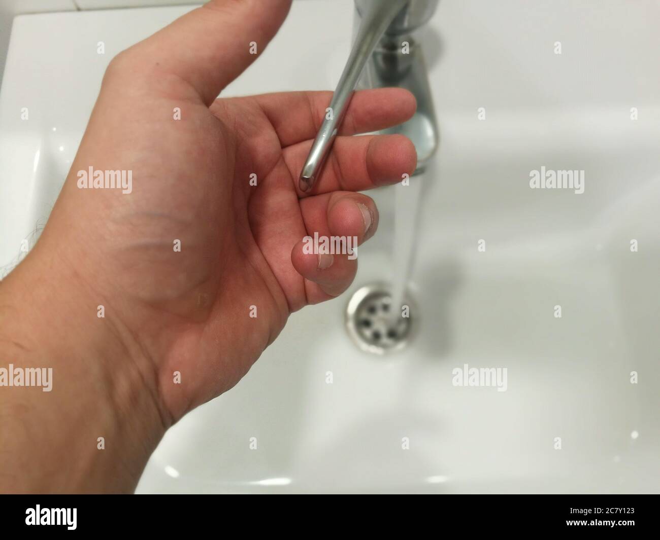 Overhead shot of running water with white ceramic sink and a male hand ...