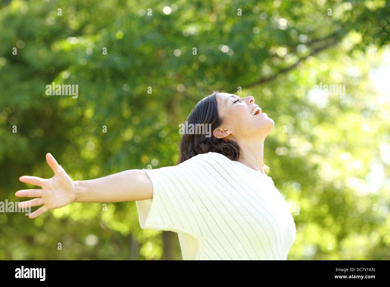 Happy adult woman breathing fresh air outstretching arms in the park at ...