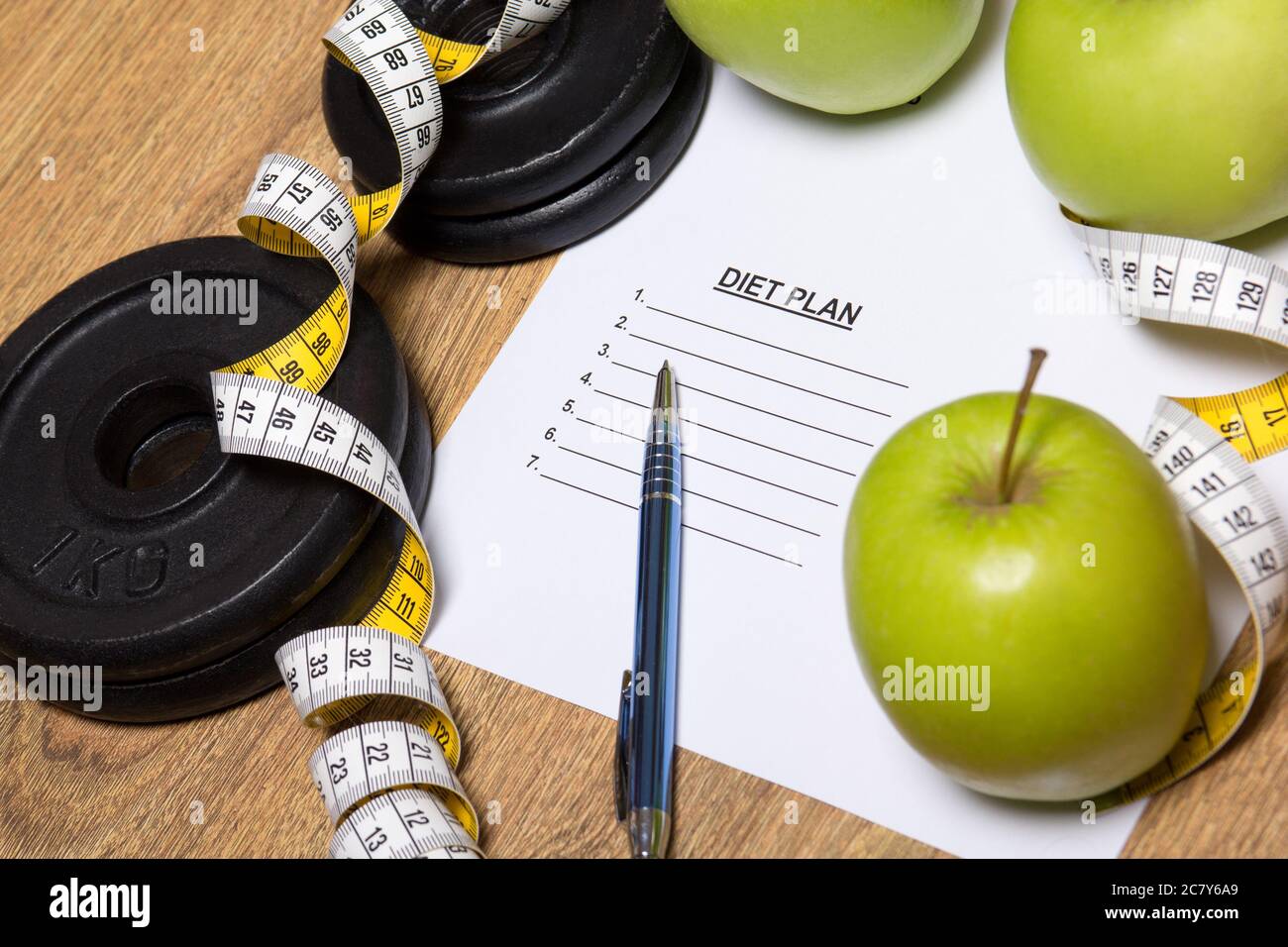 sheet of paper with diet plan, apples and dumbbell on wooden table ...