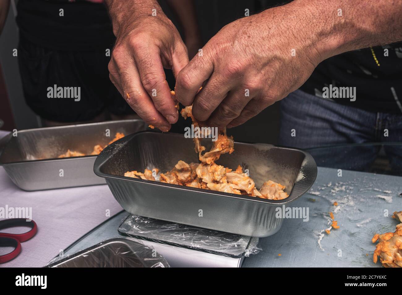 Male chef mixing red cheddar cheese and dough in a metal container on a ...