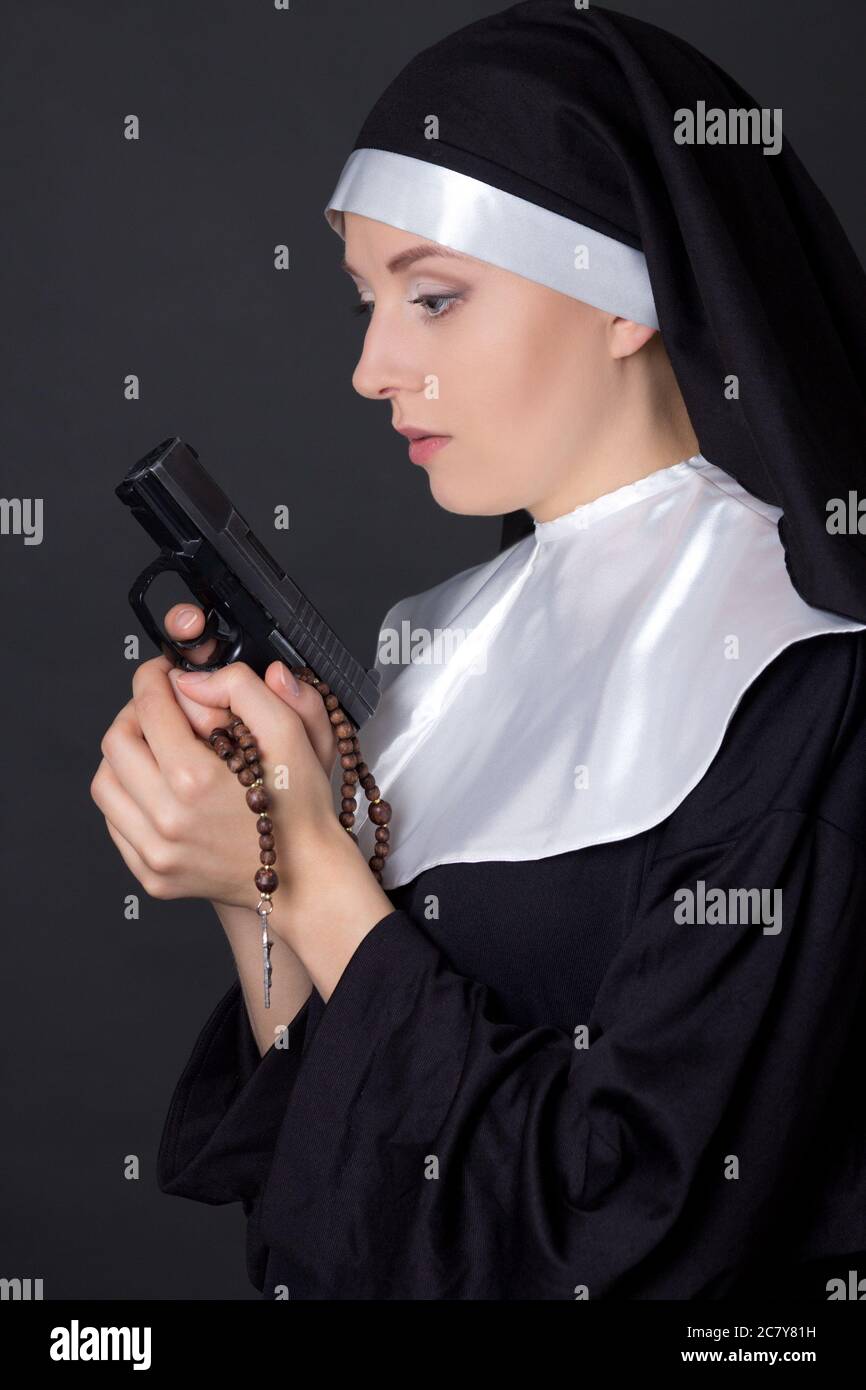 portrait of young woman nun holding gun over grey background Stock ...