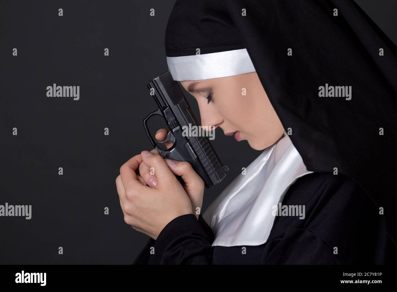 young woman nun praying with gun over grey background Stock Photo - Alamy