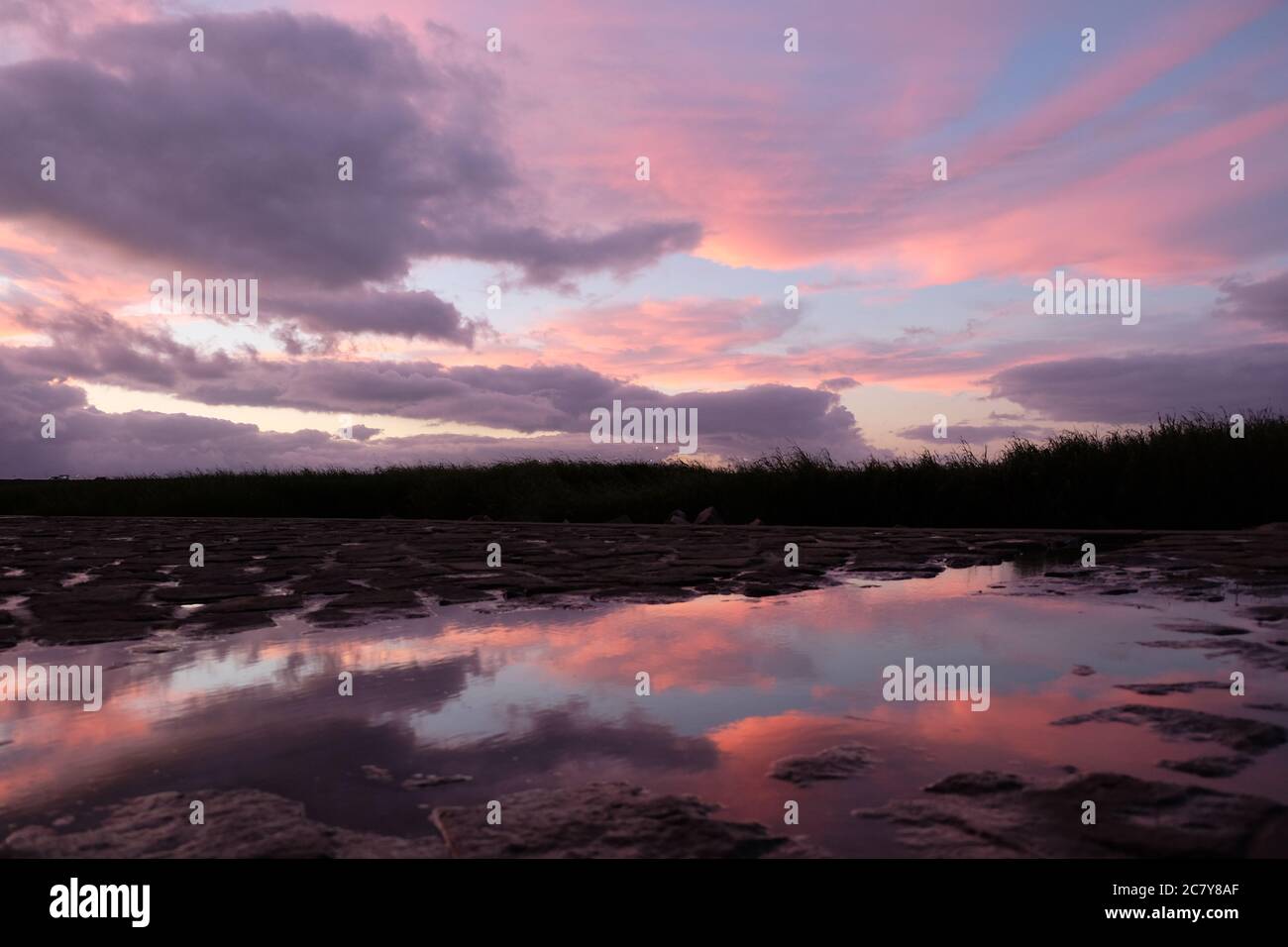colorful sunset clouds sky and reflection in puddle water. Low angle ...
