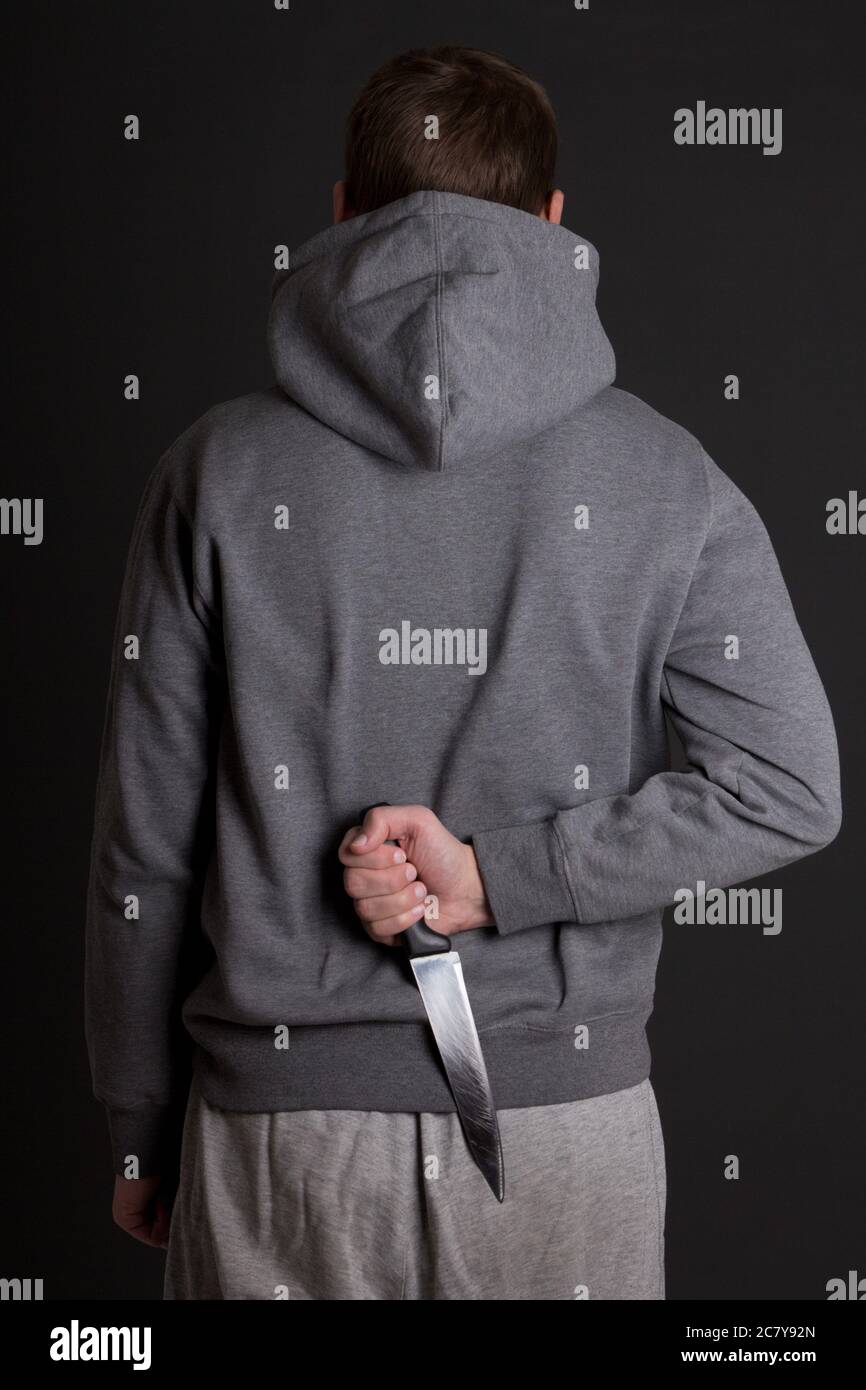 man hiding knife behind his back over grey background Stock Photo - Alamy