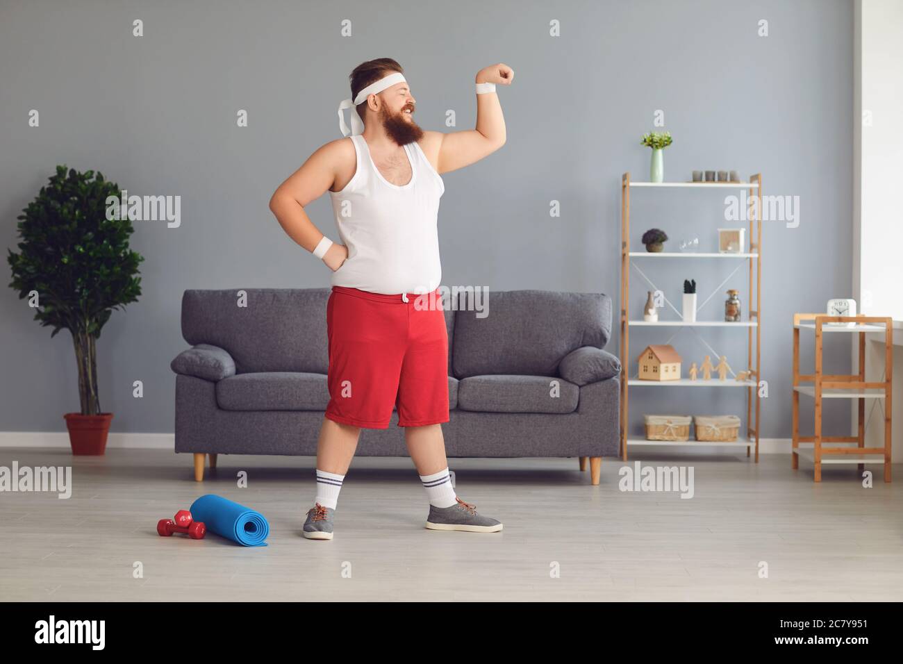 Funny fat man in sportswear shows muscles standing in the room at home ...