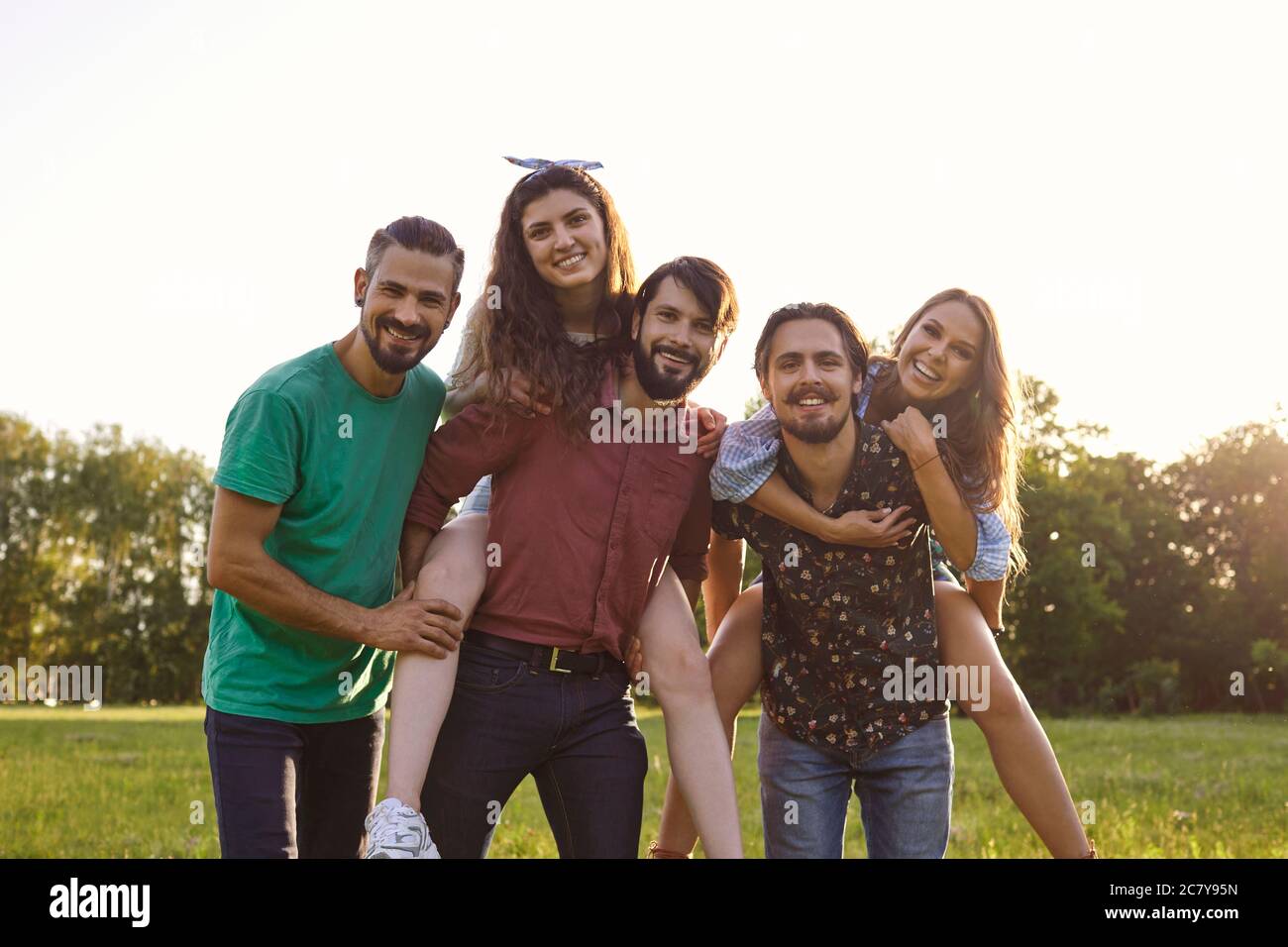 Group of happy friends piggyback ride laughing hugging on nature in ...