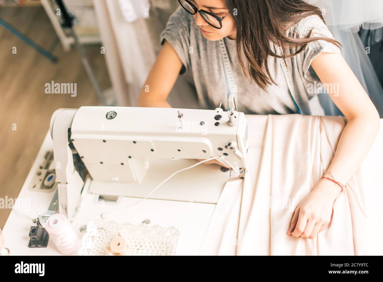 Young woman sewing with sewing machine at studio while sitting at her ...