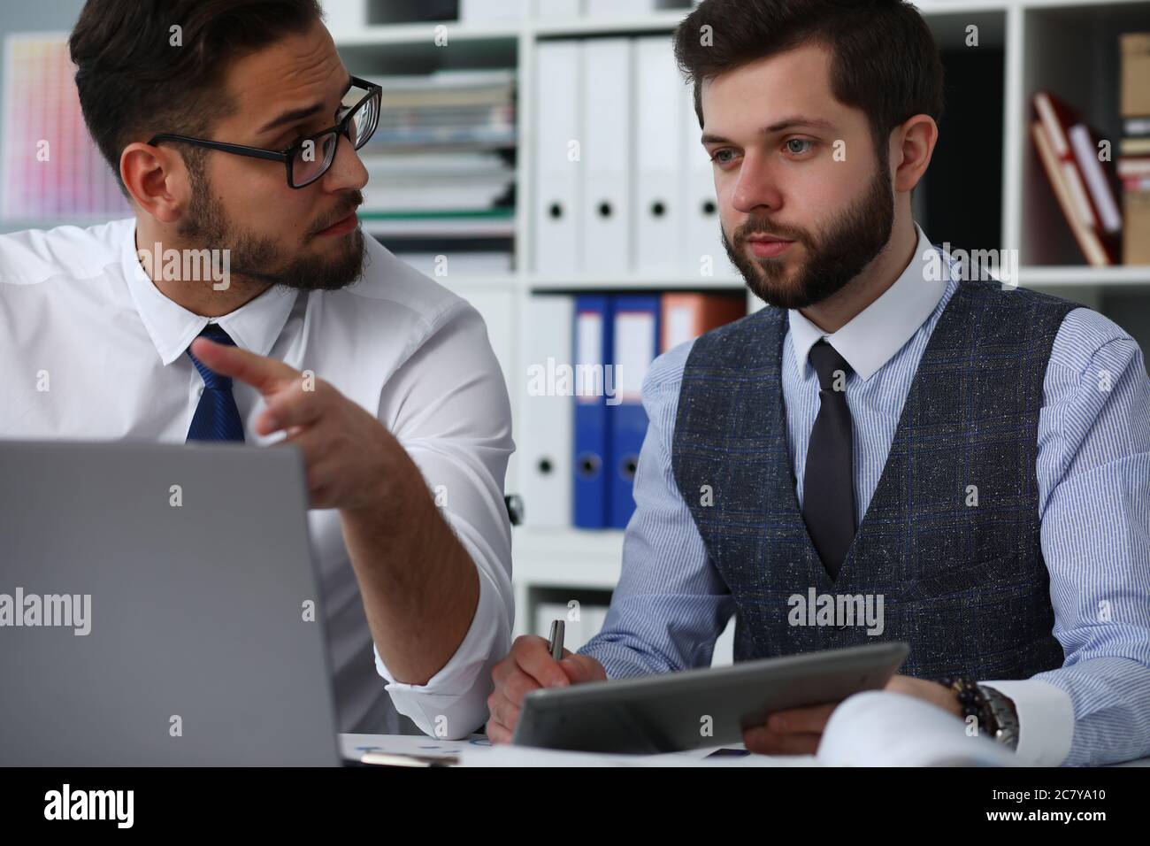 Two men in office using laptop and communicating Stock Photo - Alamy