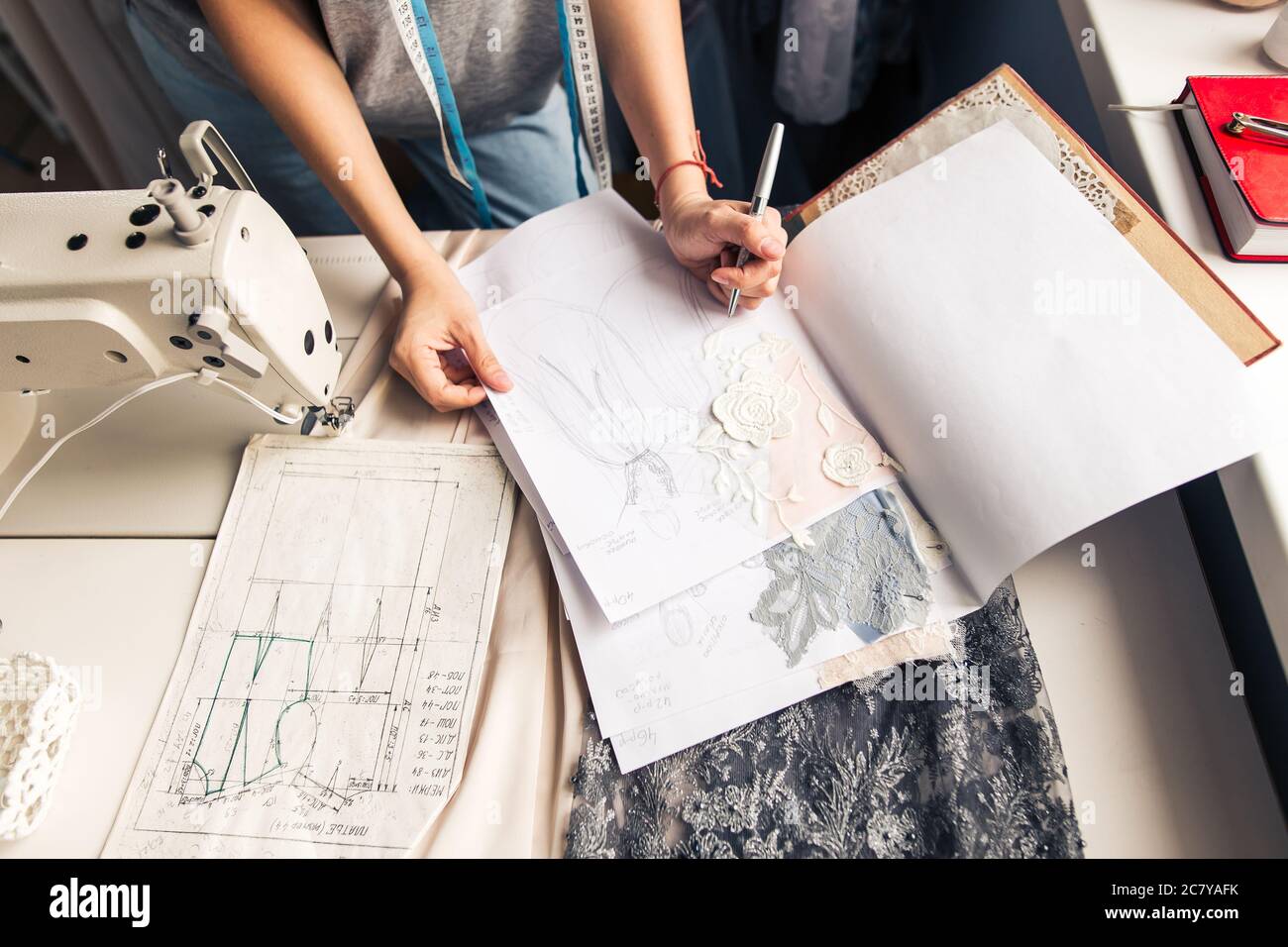 Focused attractive young woman tailor standing and drawing on textile ...