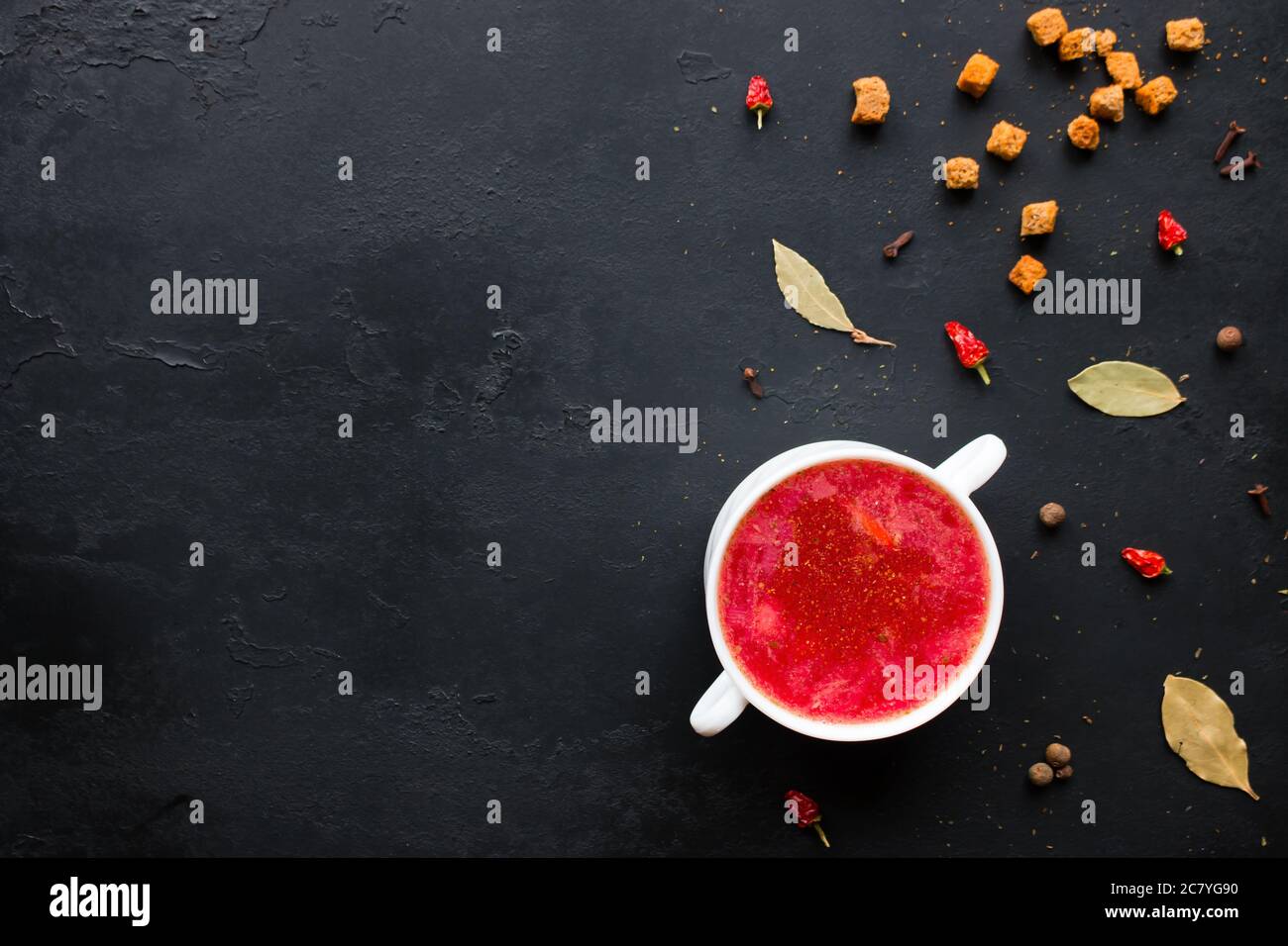 Borscht in a white plate with herbs, spices and rusks on a black ...