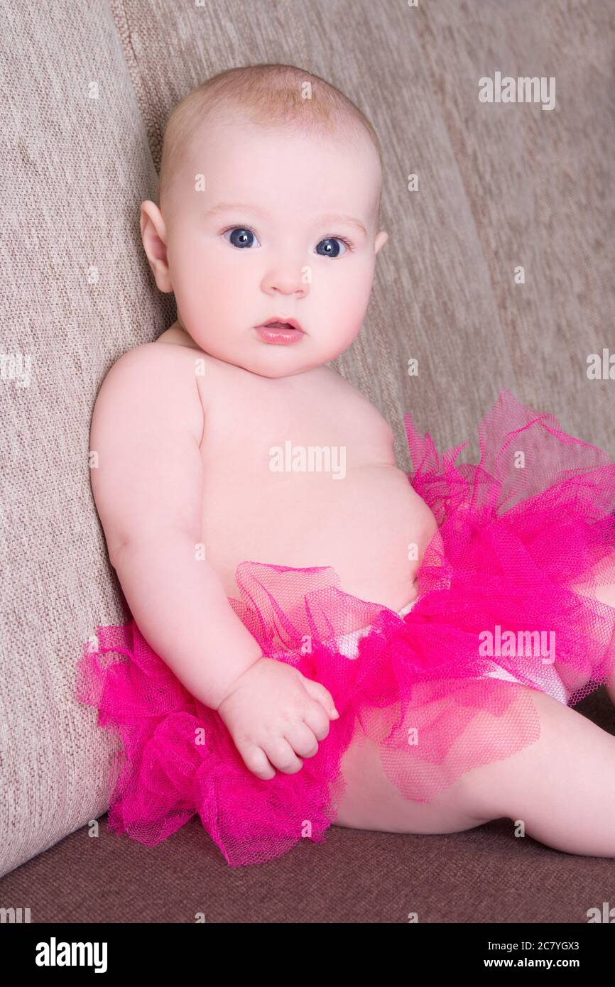 funny baby girl in pink skirt sitting on the sofa Stock Photo - Alamy