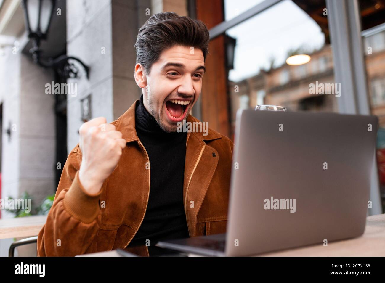 Young cheerful casual man joyfully showing yes gesture while working on ...