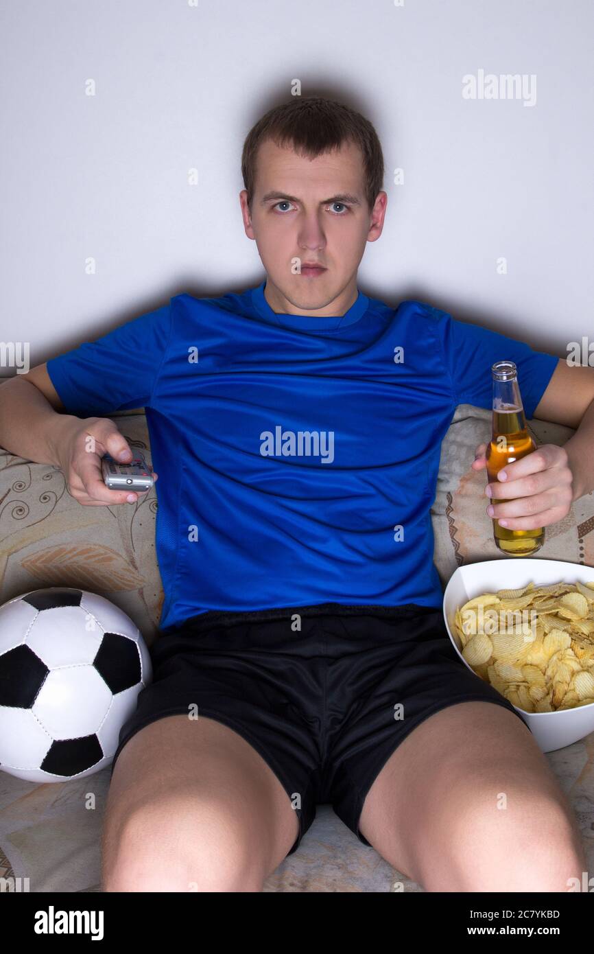 bored man in football uniform sitting in living room and watching tv ...