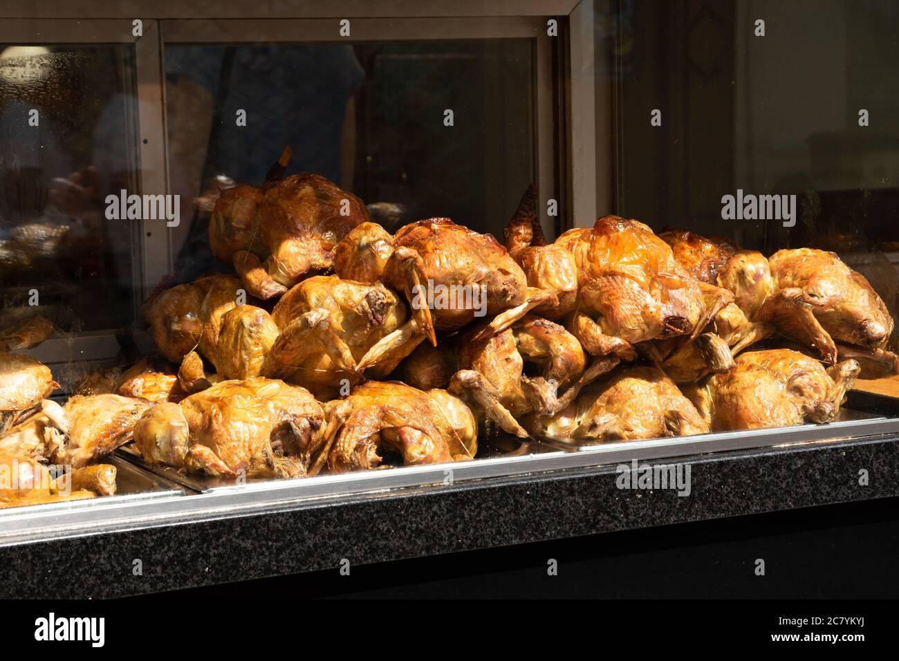 Grilled appetizing chicken in rotisserie machine at entrance to butcher ...