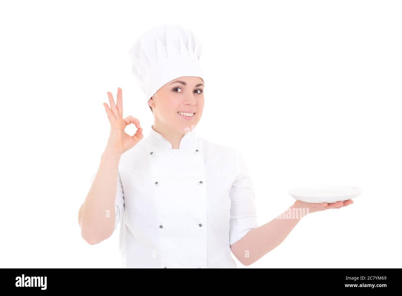 portrait of young cook woman in uniform with empty plate showing ok ...