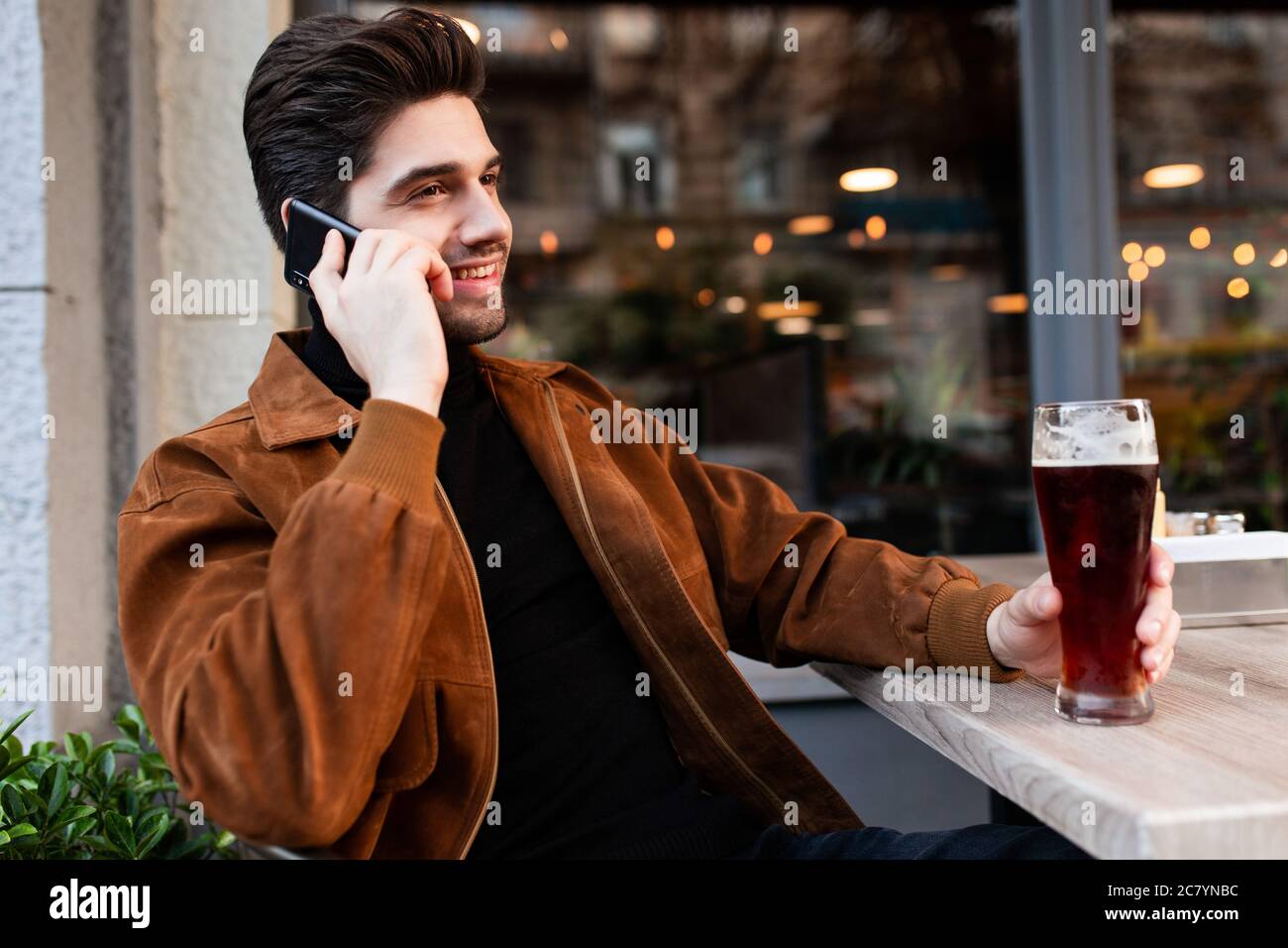 Young handsome man happily talking on cellphone sitting with beer in ...