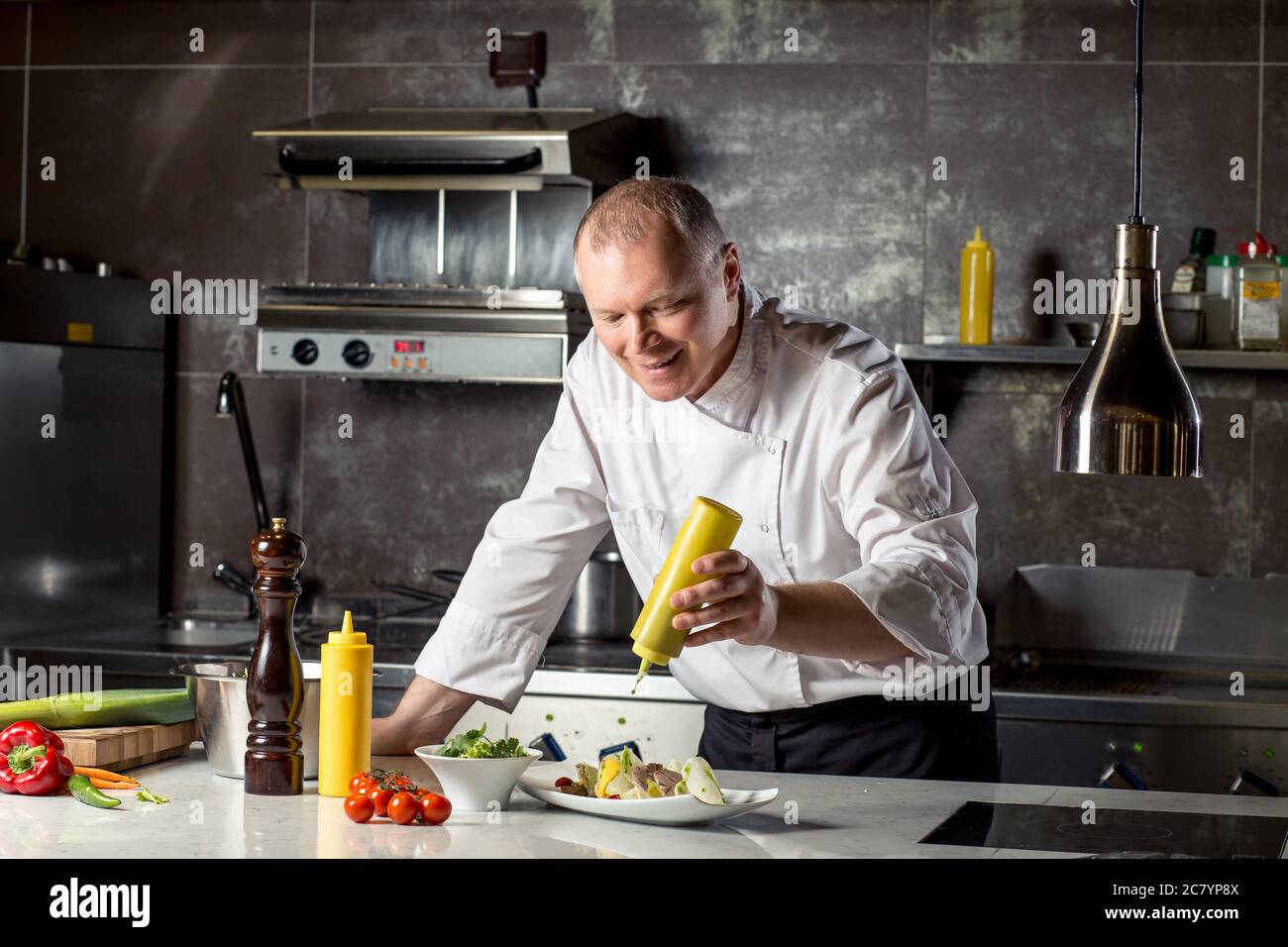 Chef plating up food in a restaurant pouring a gravy or sauce over the ...