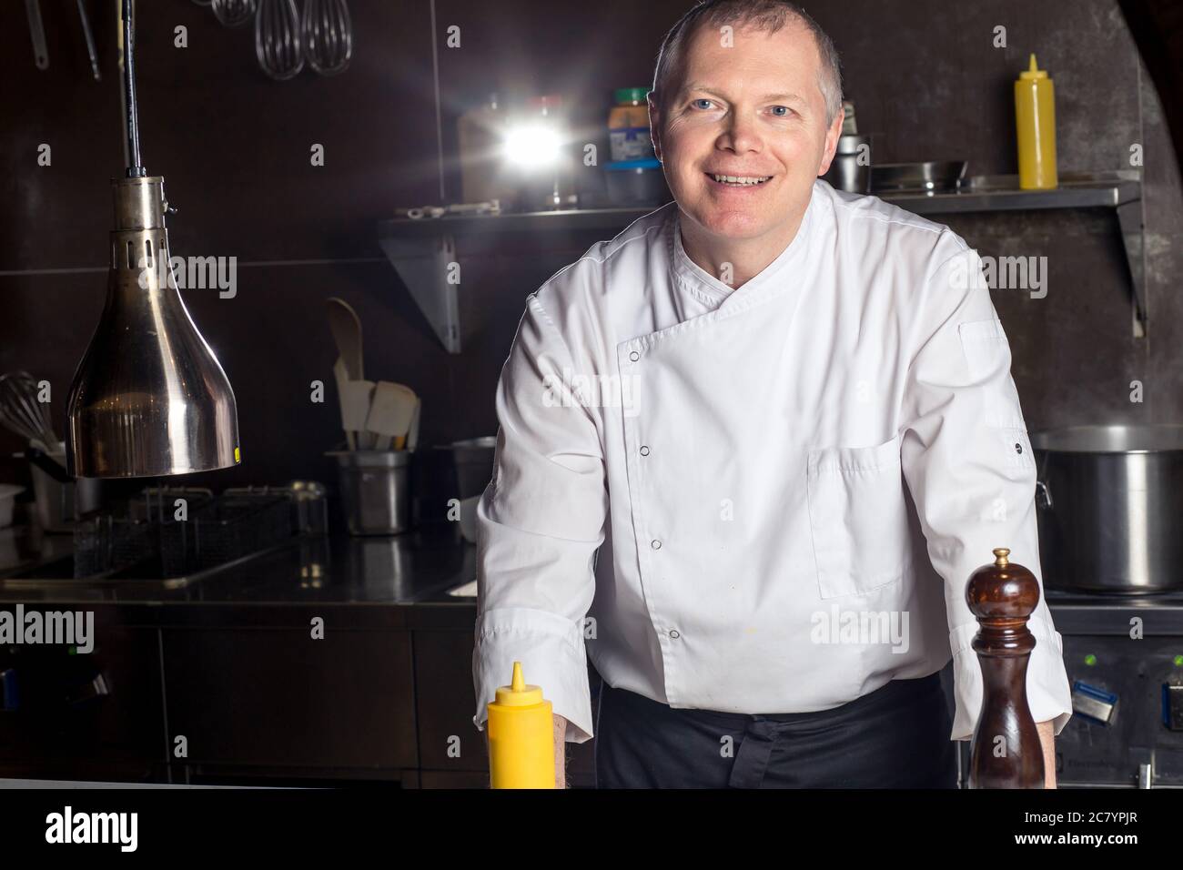 Chef leaning on the counter with a dish in a commercial kitchen Stock ...