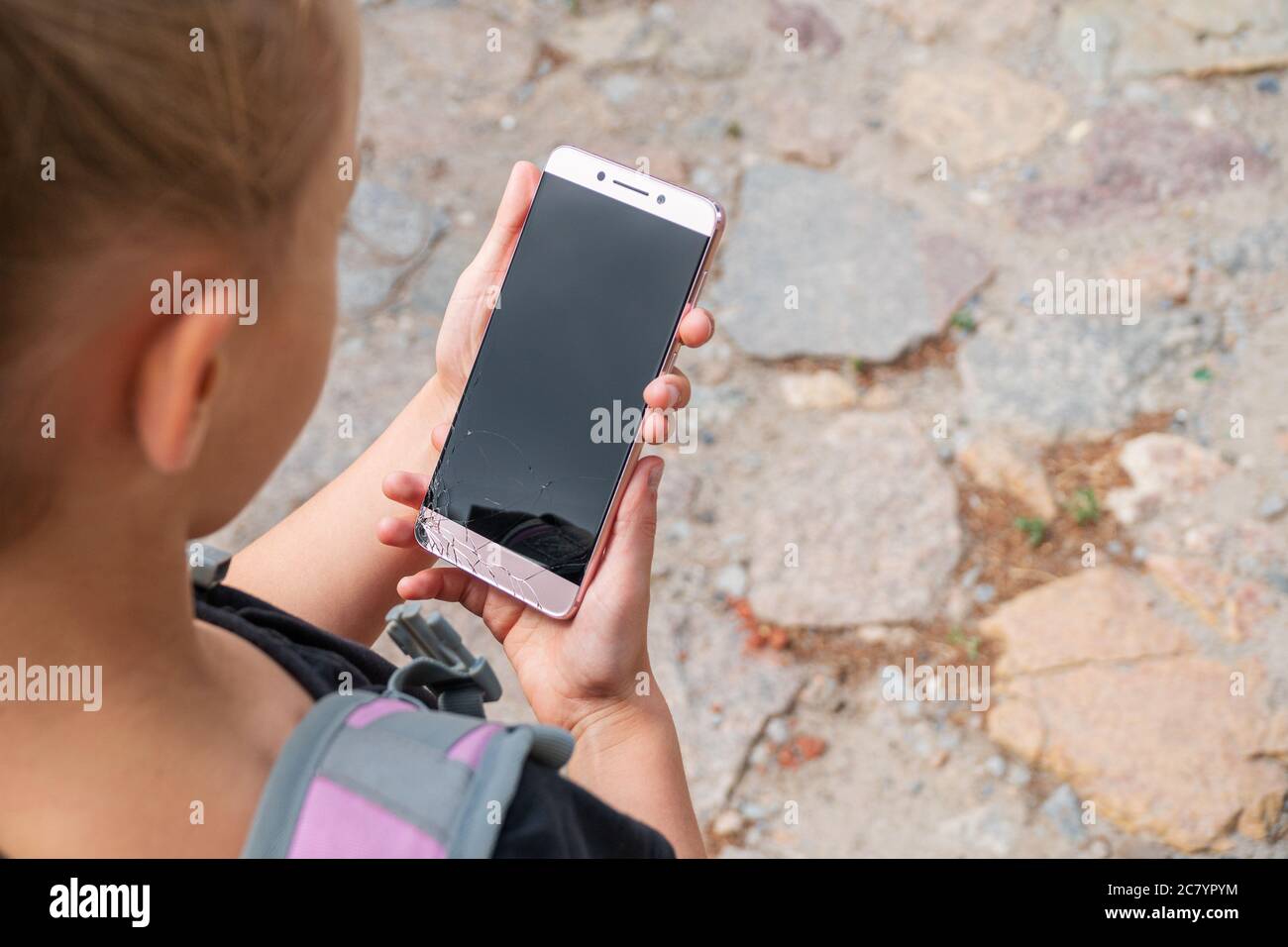 little girl holding a phone with broken screen while going to school ...