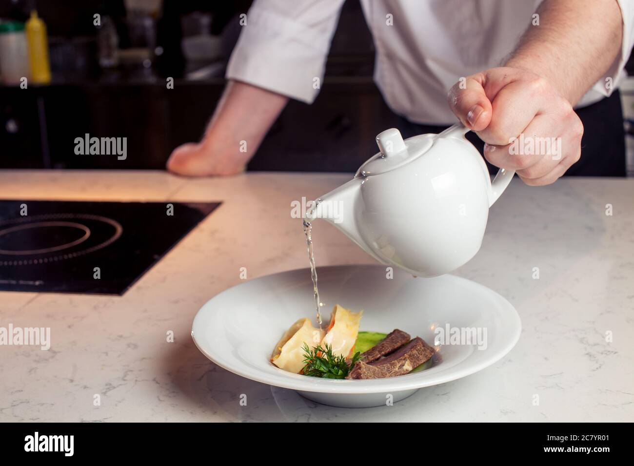 Chef plating up food in a restaurant pouring a gravy or sauce over the ...