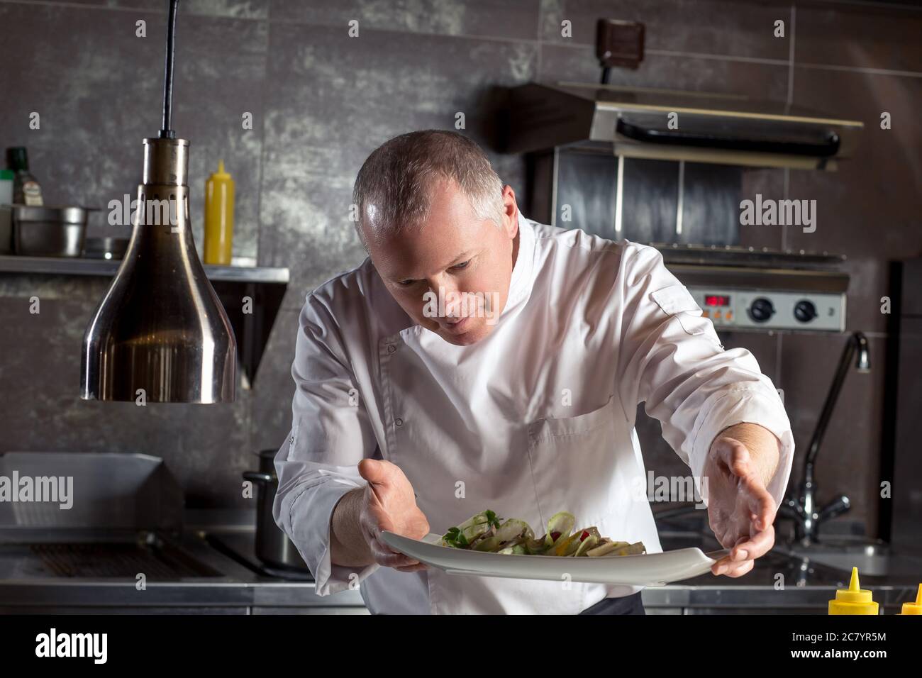 Happy chef sprinkling cheese on a pizza in a commercial kitchen Stock ...