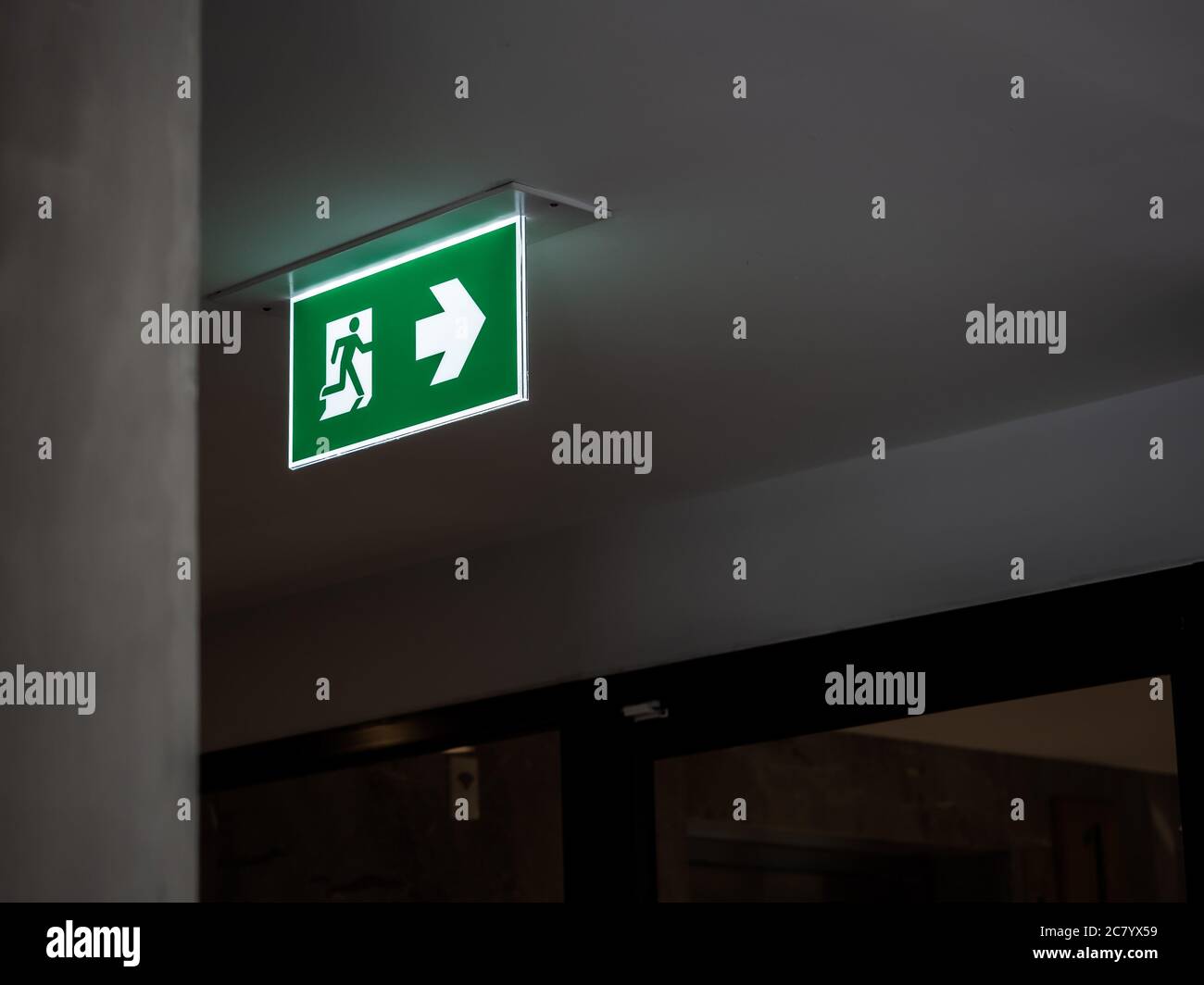 Fire exit. Illuminated green emergency exit sign hanging on ceiling in ...