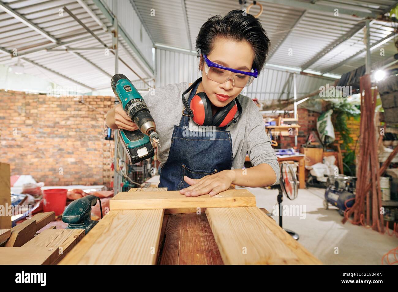 Young Asian female carpenter using drill when assembling bookshelf or ...