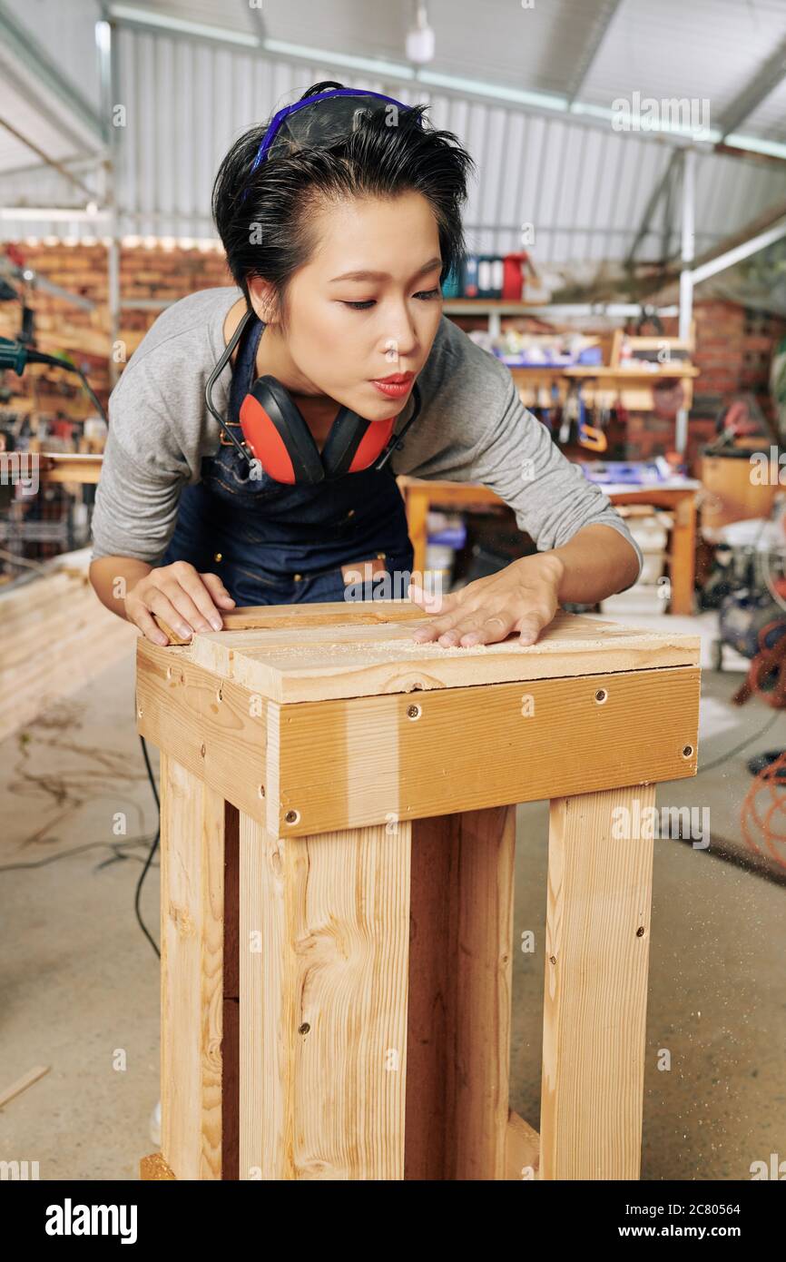 Vietnamese female carpenter blowing away wooden shavings from furniture ...