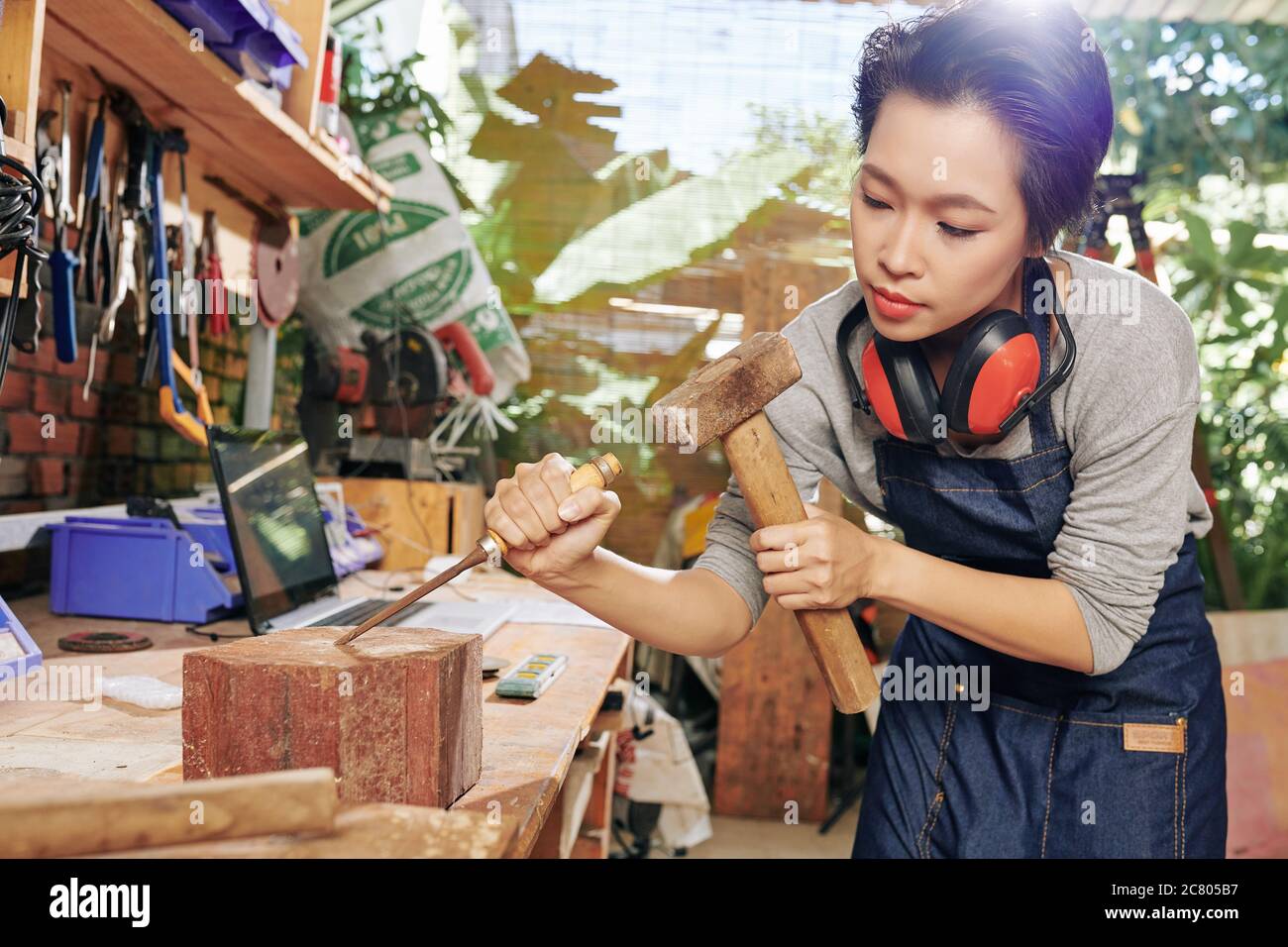 Concentrated Vietnamese carpenter using chisel and hammer when carving ...