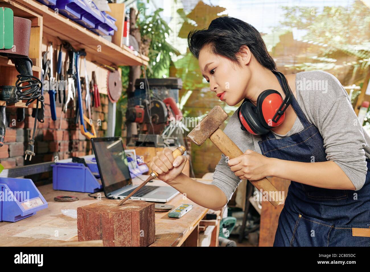 Vietnamese female carpenter using chisel and hammer when working with ...