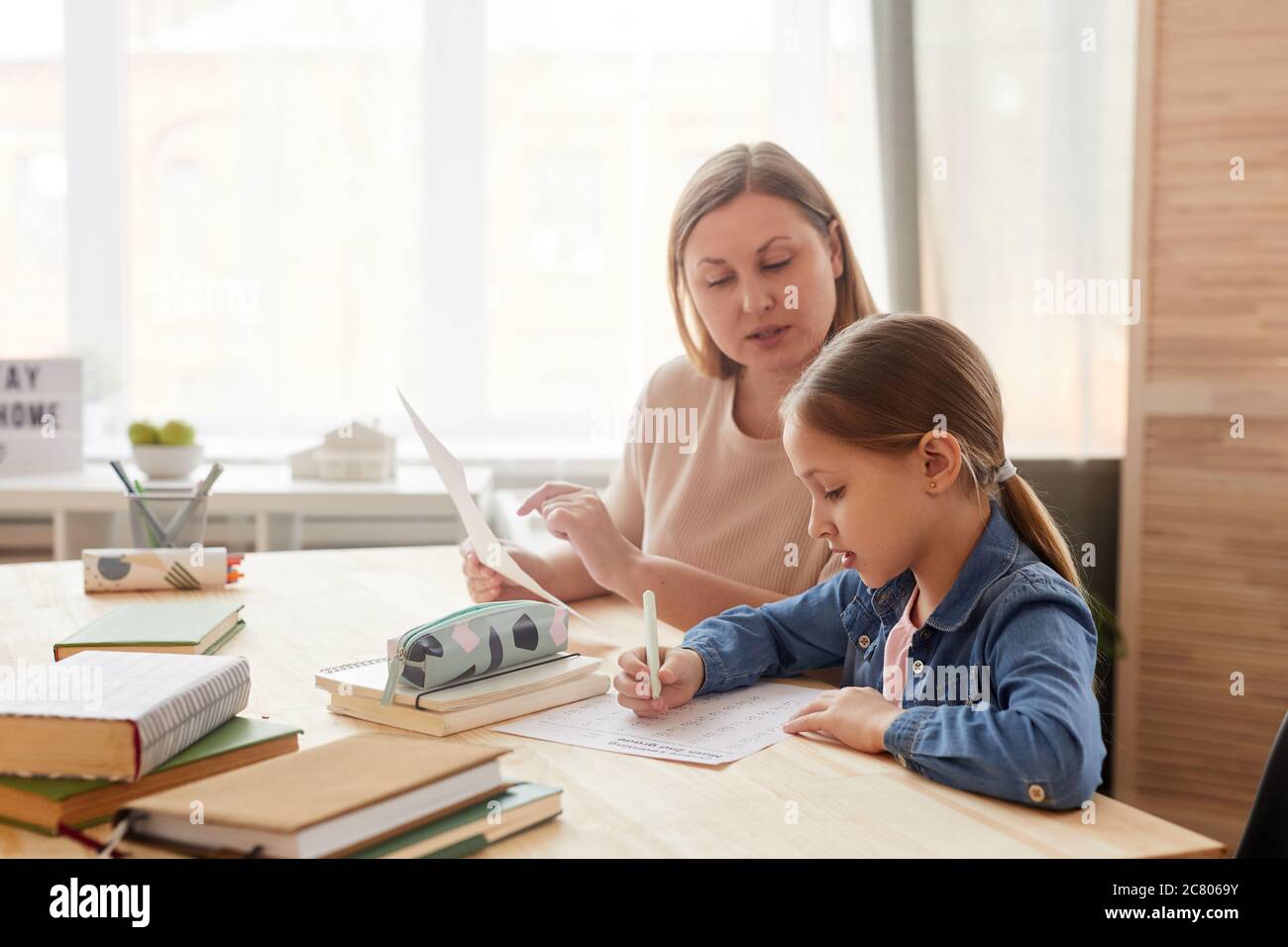 Warm-toned side view portrait of cute little girl writing test while ...