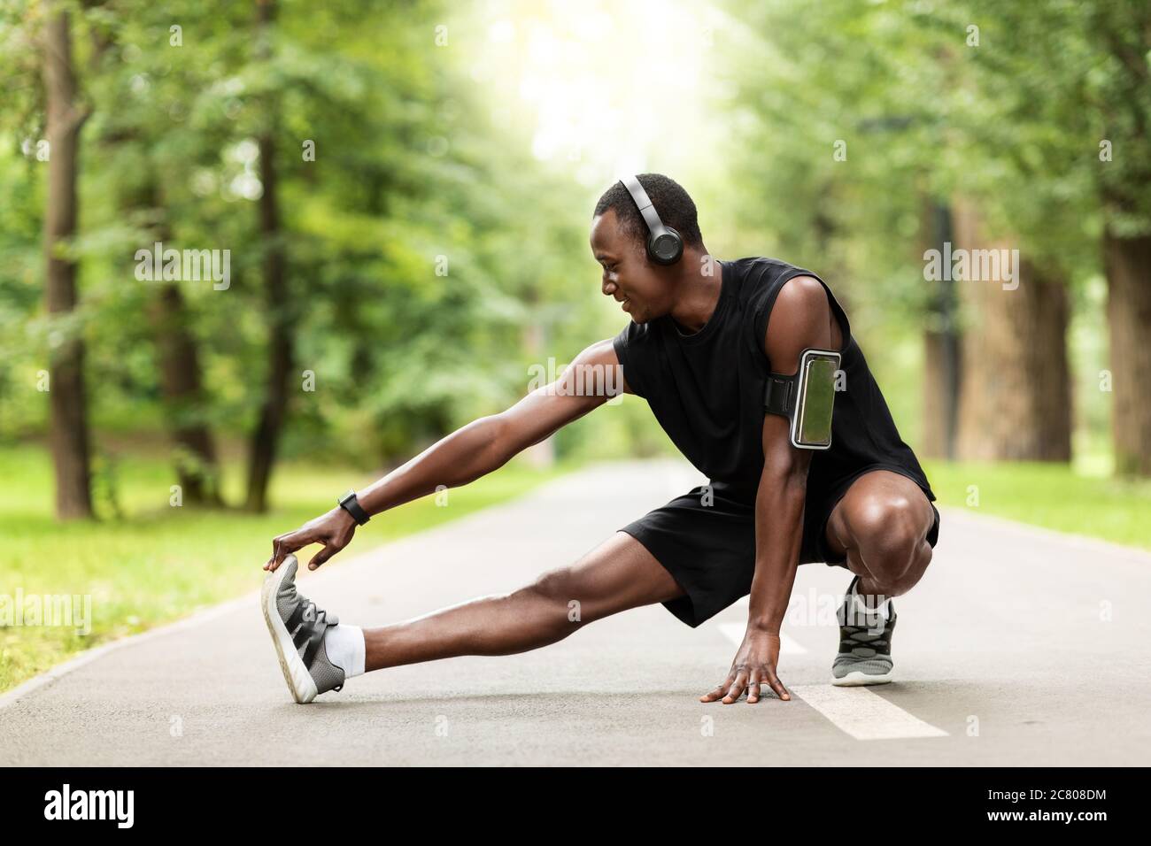 Sporty african guy stretching legs, training at park Stock Photo - Alamy
