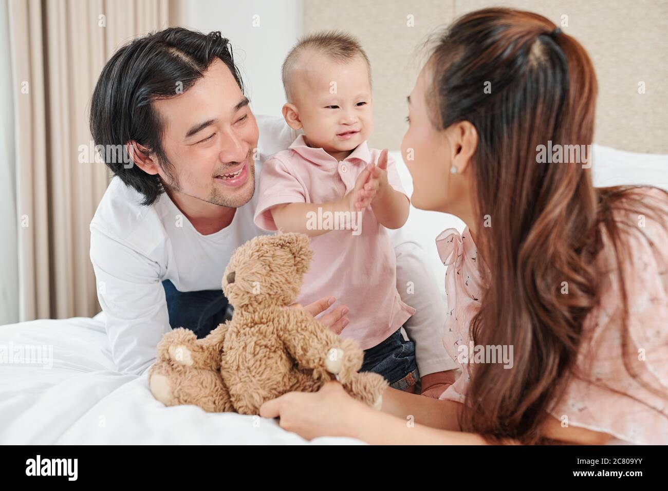 Young Asian parents playing with their little kid when resting on bed ...