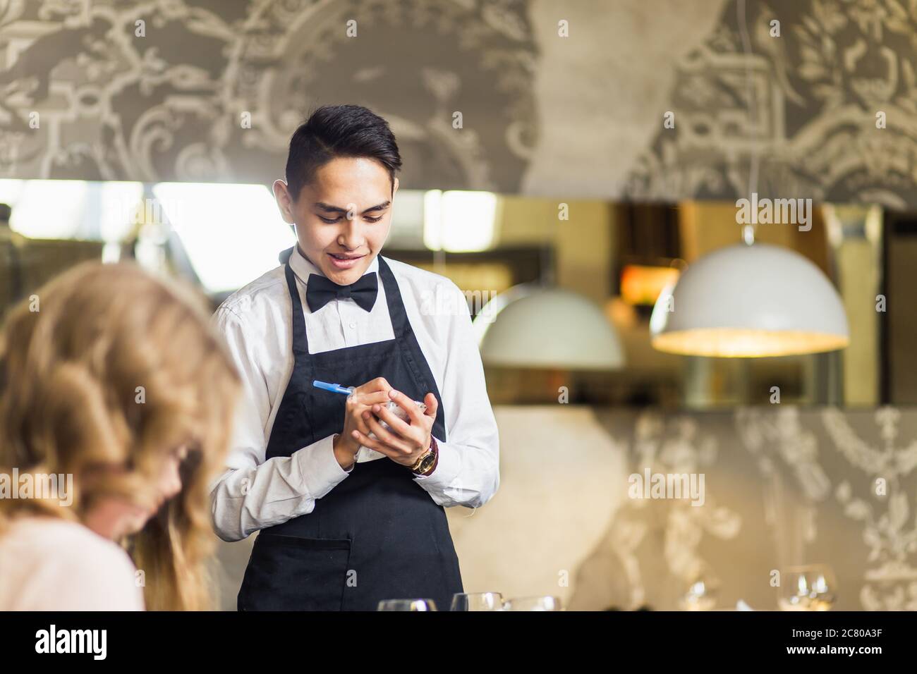 Positive young waiter serving terrace restaurant guests at table.Focus ...