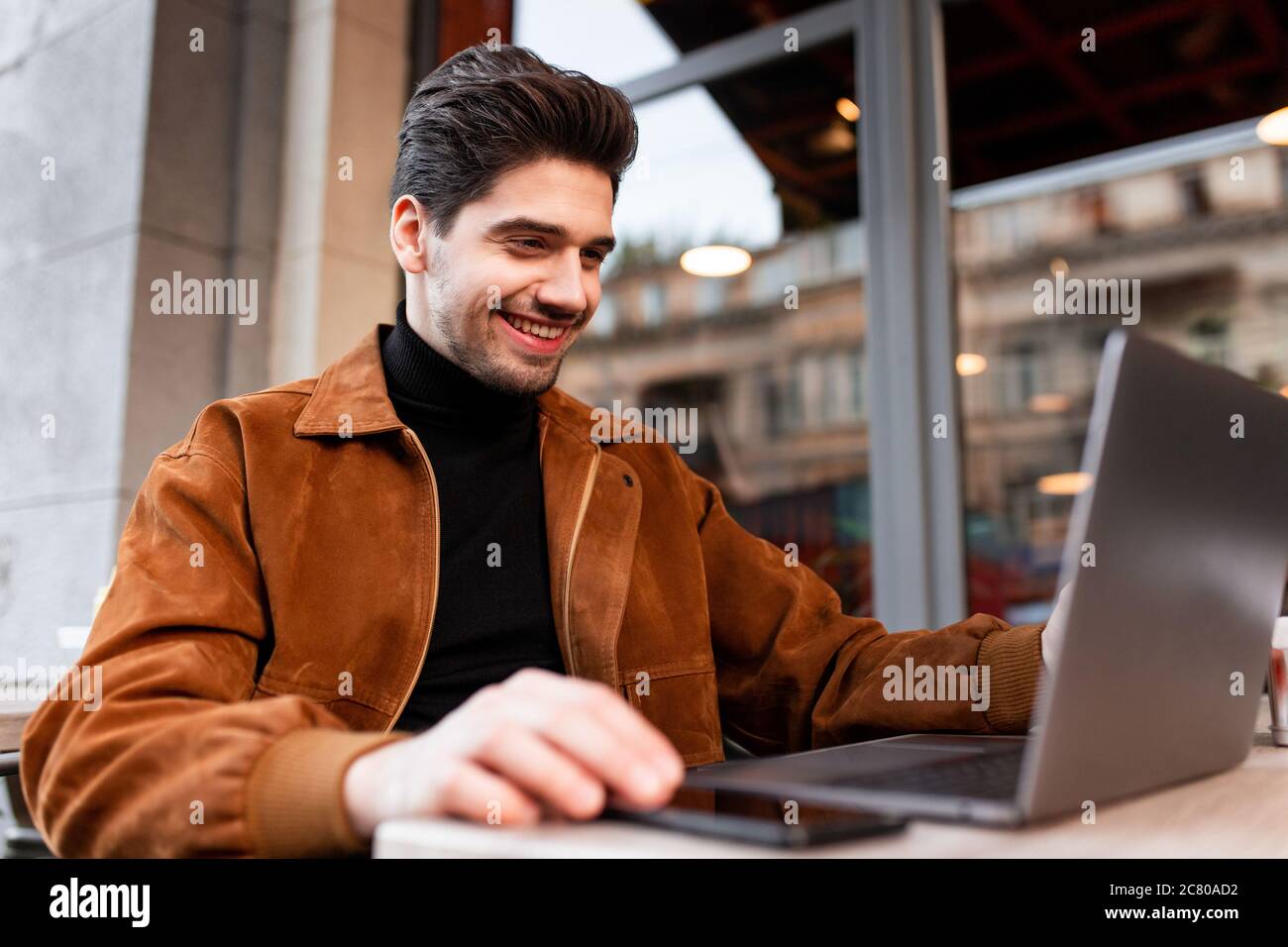 Young handsome casual businessman joyfully working on laptop in cafe on ...