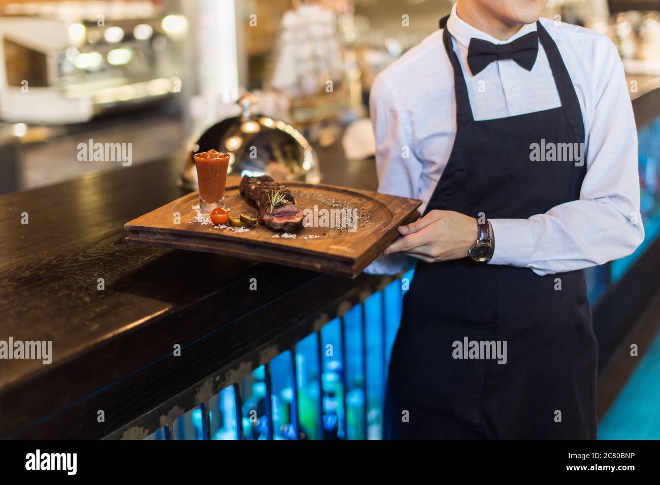 Positive young waiter serving terrace restaurant guests at table.Focus ...