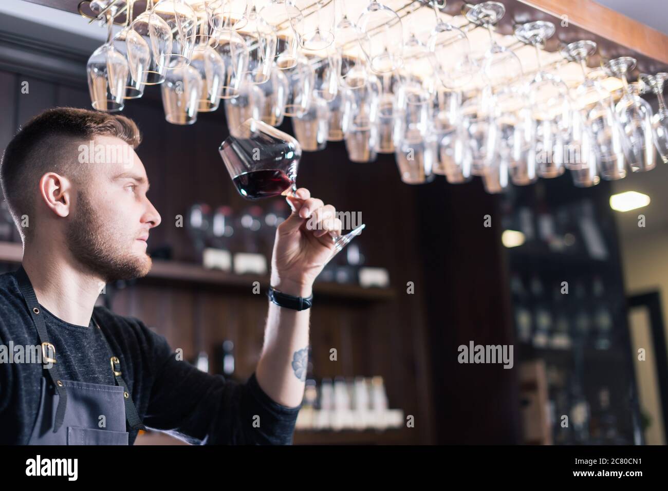 Focused young male sommelier in suite looking at red wine in glass over ...